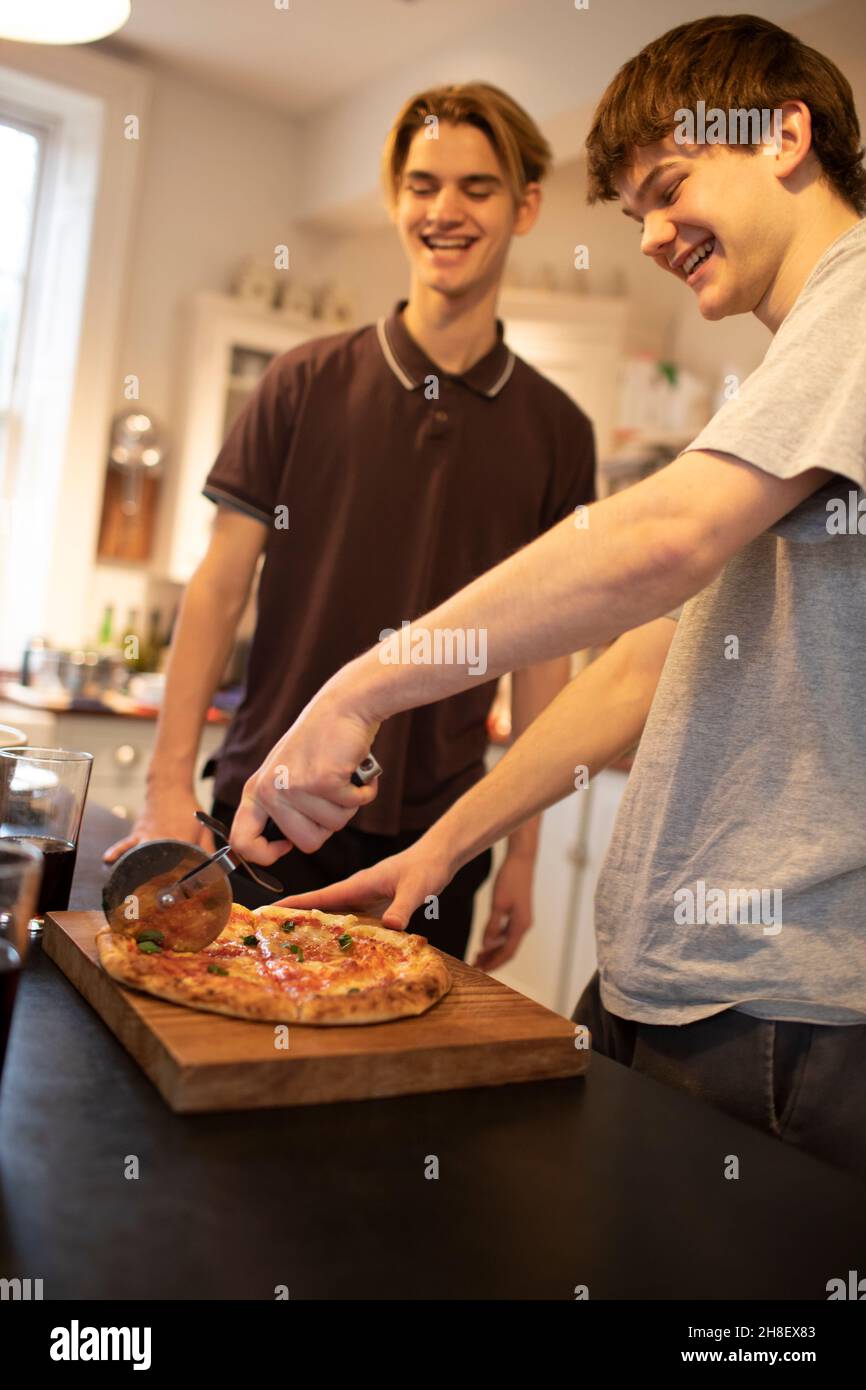 Happy teenage boys slicing fresh pizza in kitchen Stock Photo - Alamy