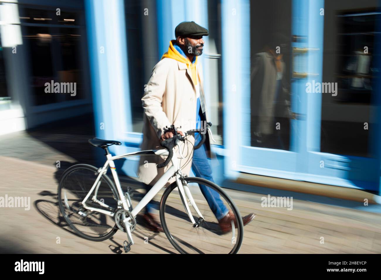 Man walking bicycle along sunny storefront Stock Photo - Alamy