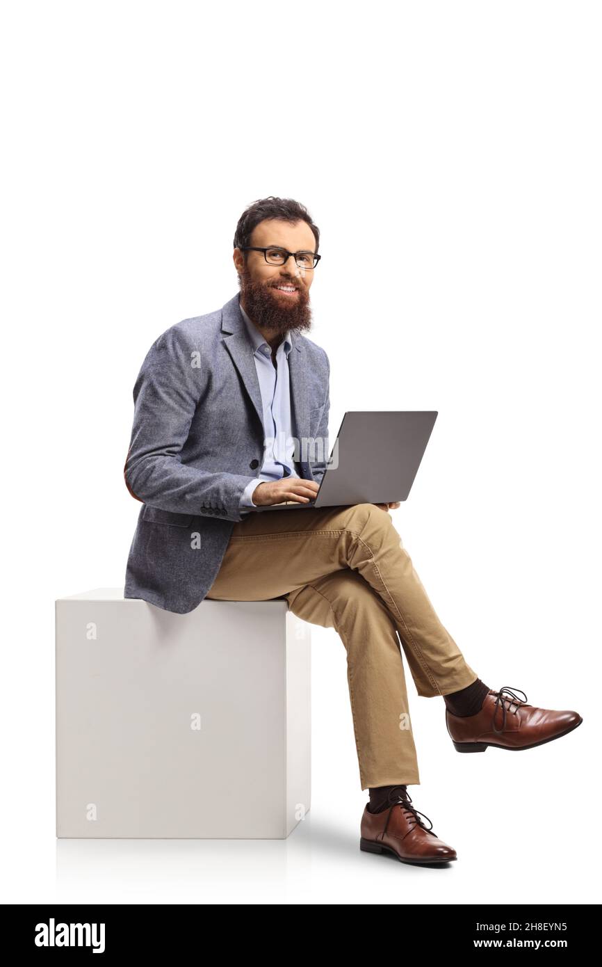 Bearded man sitting on a white cube and using a laptop computer ...