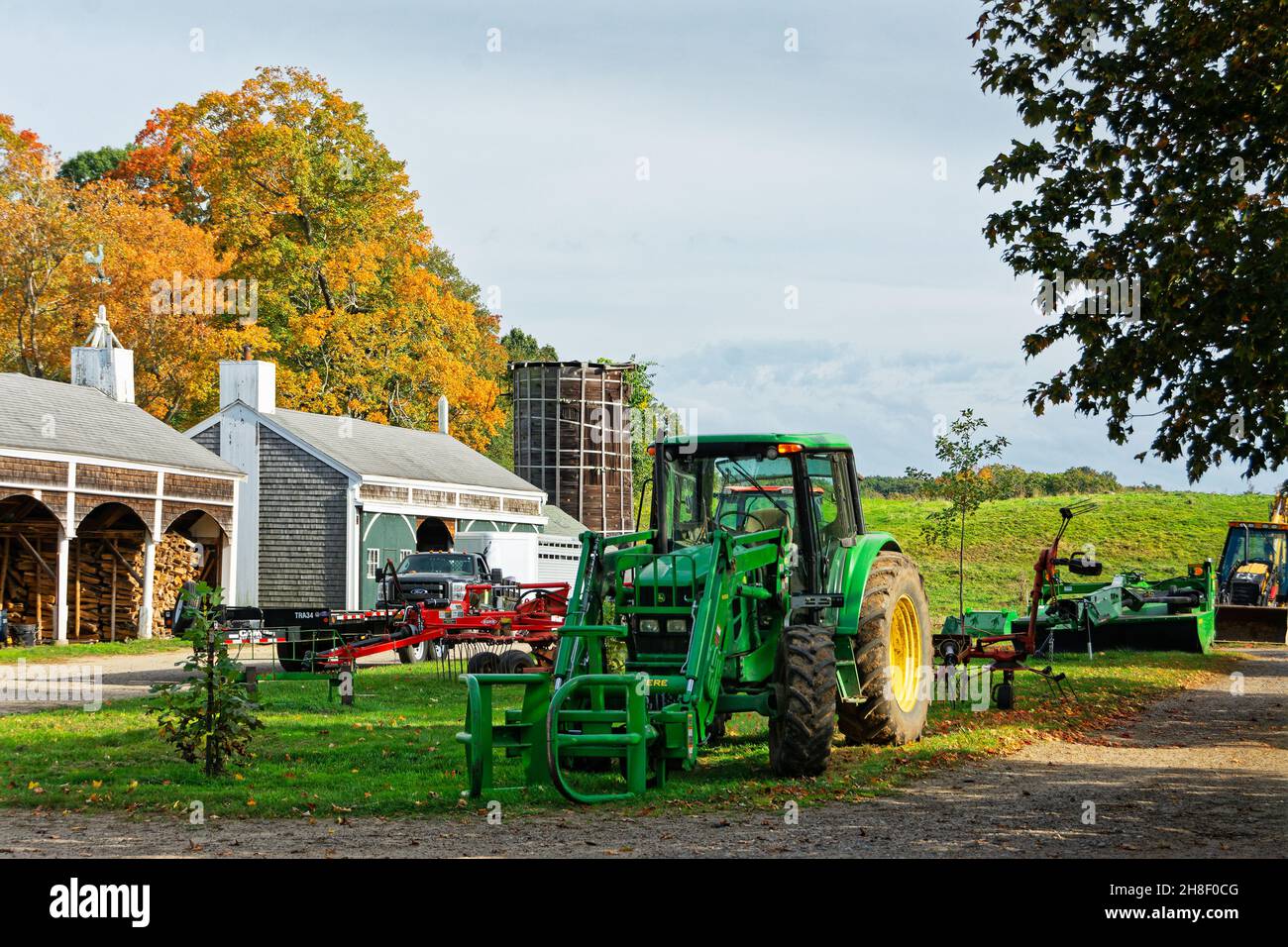 A bright green John Deere tractor sits in the grass in front of barns ...