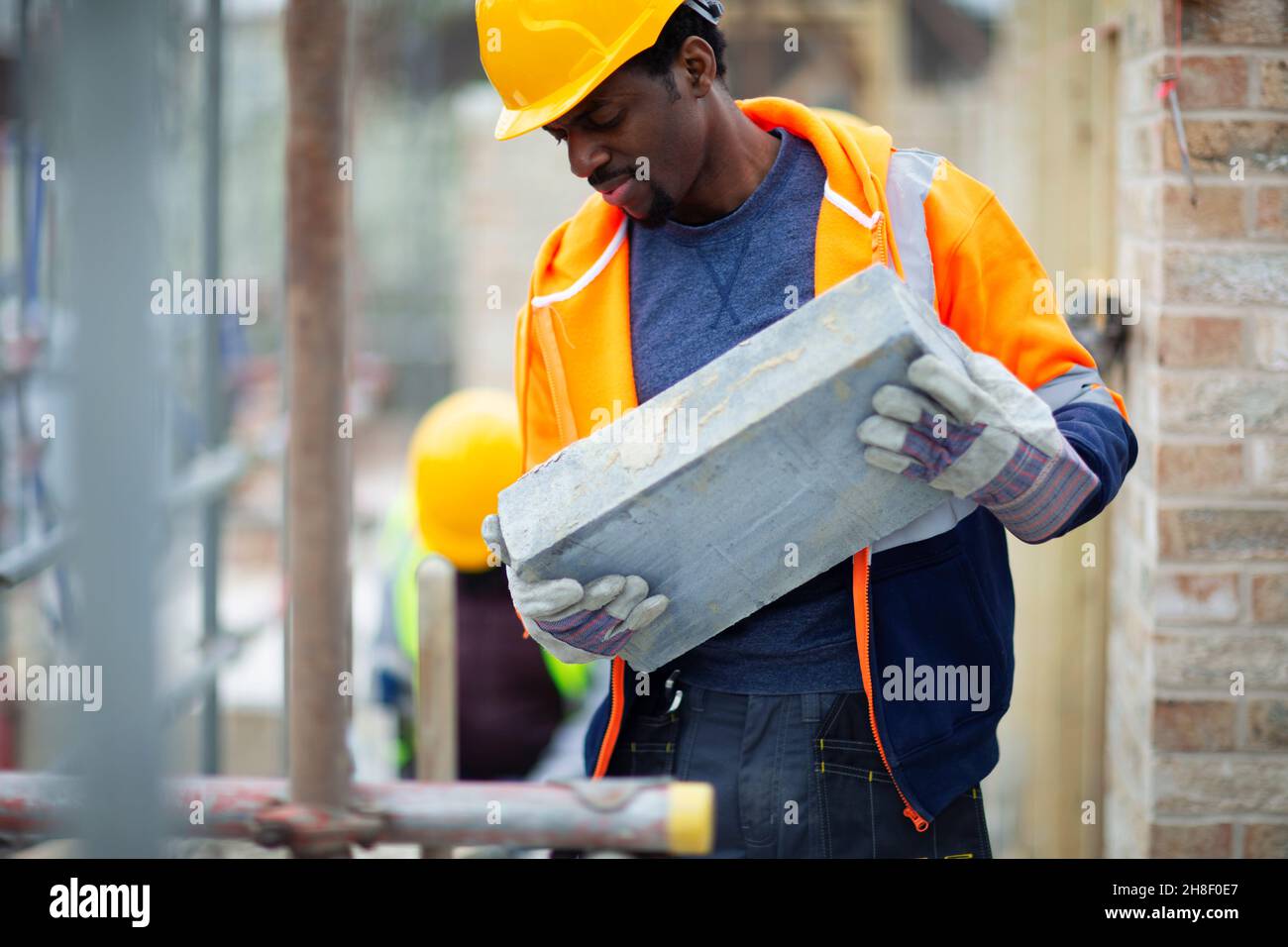 Construction worker carrying brick at construction site Stock Photo - Alamy