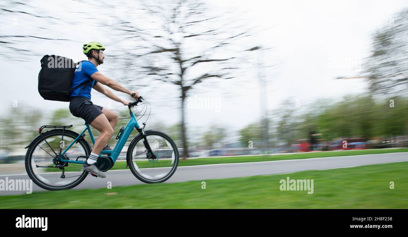 Male delivery man riding bicycle in urban park Stock Photo - Alamy