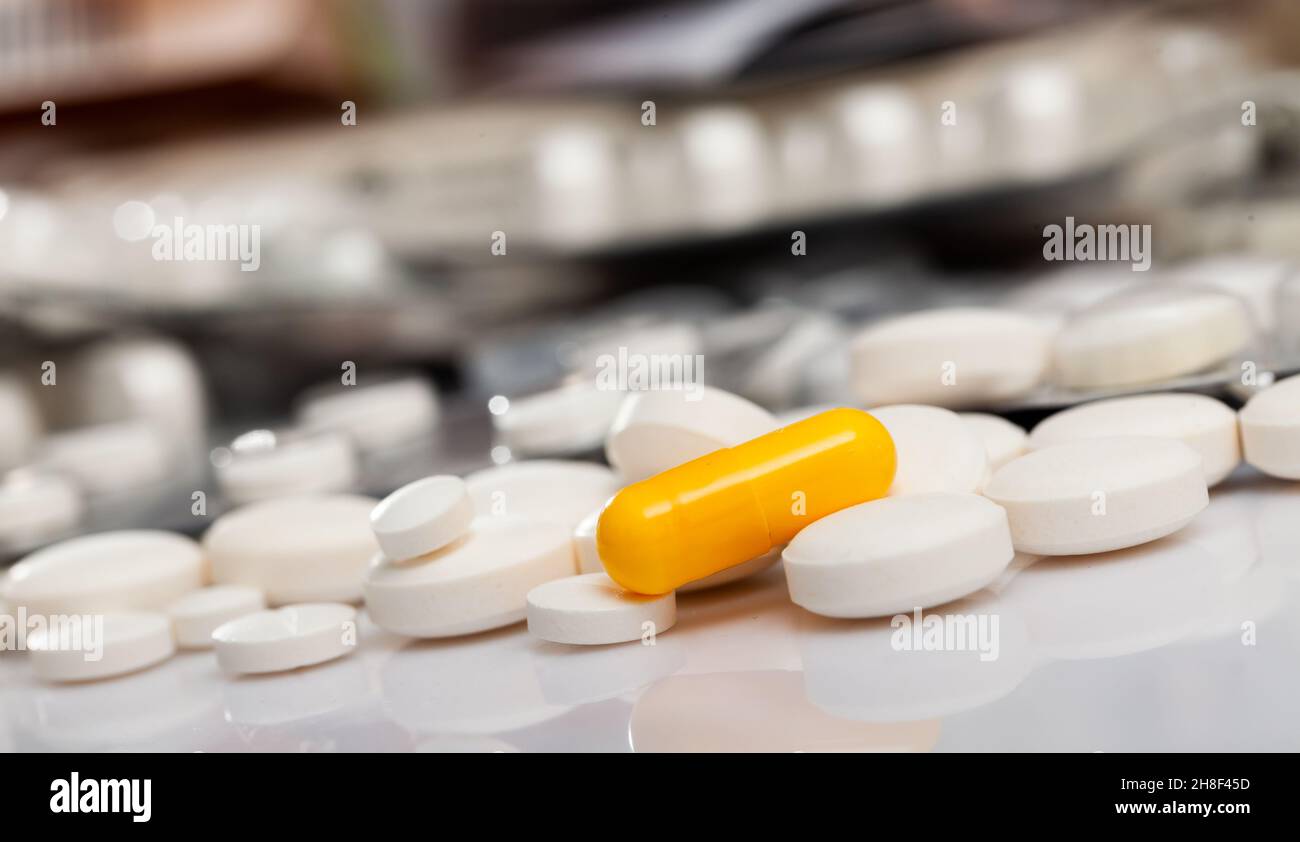 Yellow drug capsule among white tablets Stock Photo - Alamy