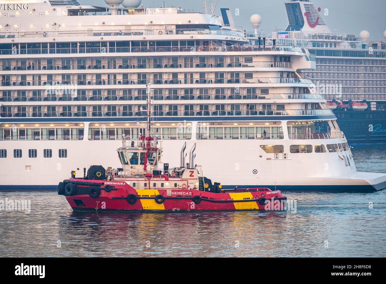 red and yellow tug boat next to a large cruise ship Stock Photo - Alamy