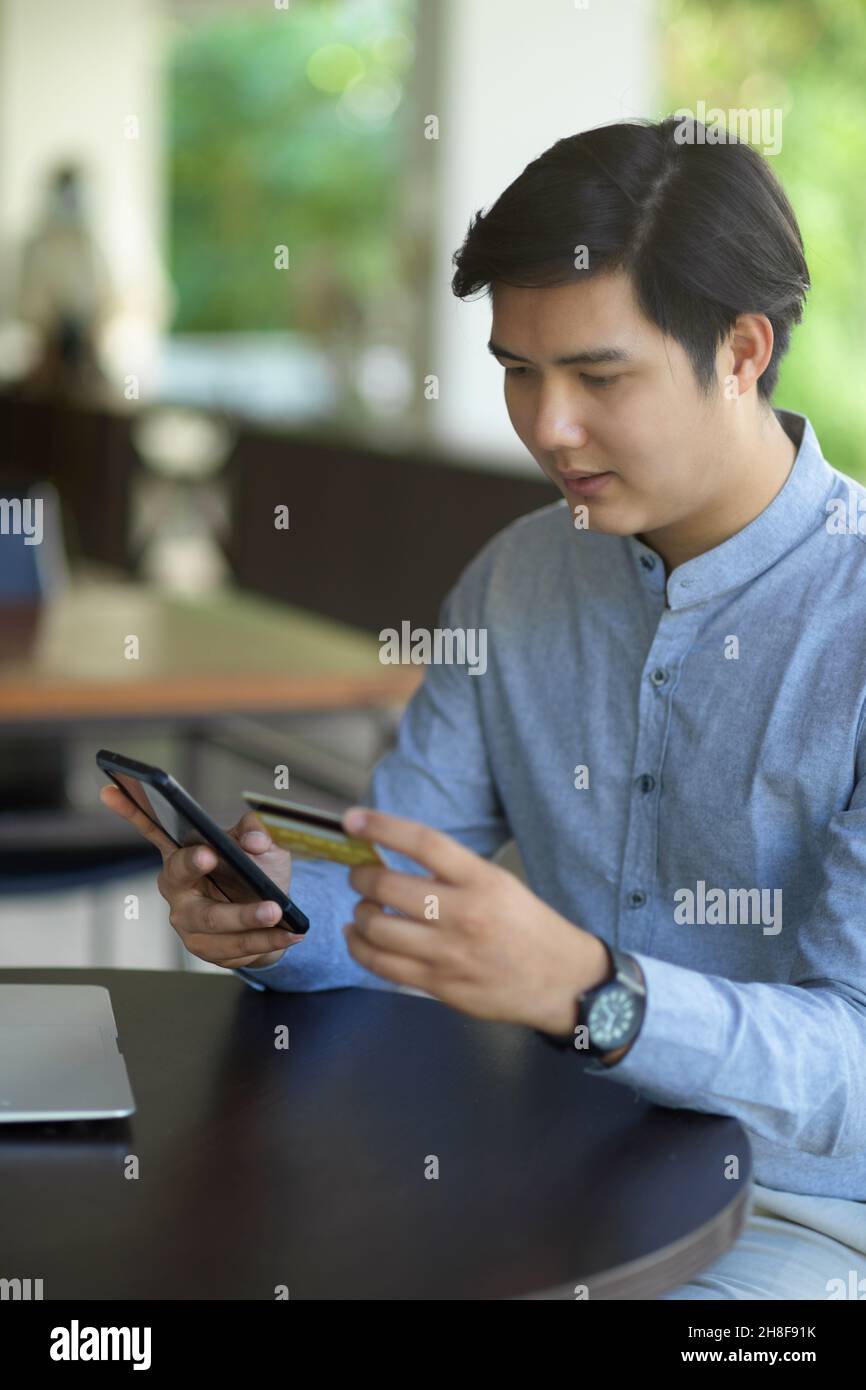 An asian man using his smartphone to connect with his credit card via ...