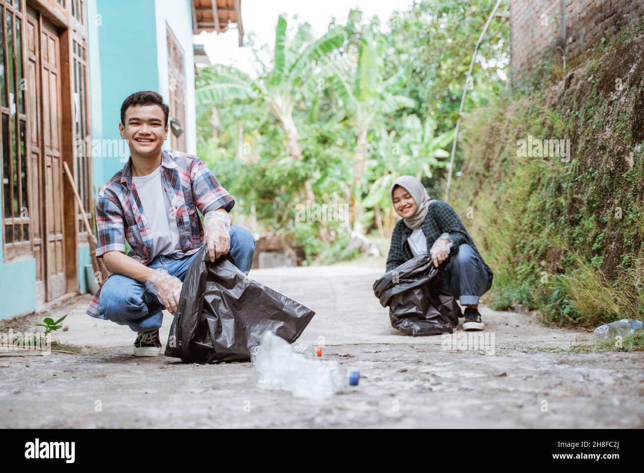 two happy teenage volunteers picking up trash Stock Photo - Alamy