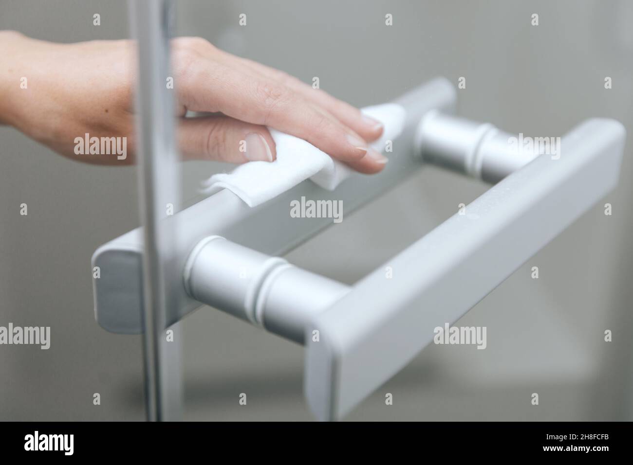 Cleaning glass door handles with an antiseptic wet wipe. Woman hand ...