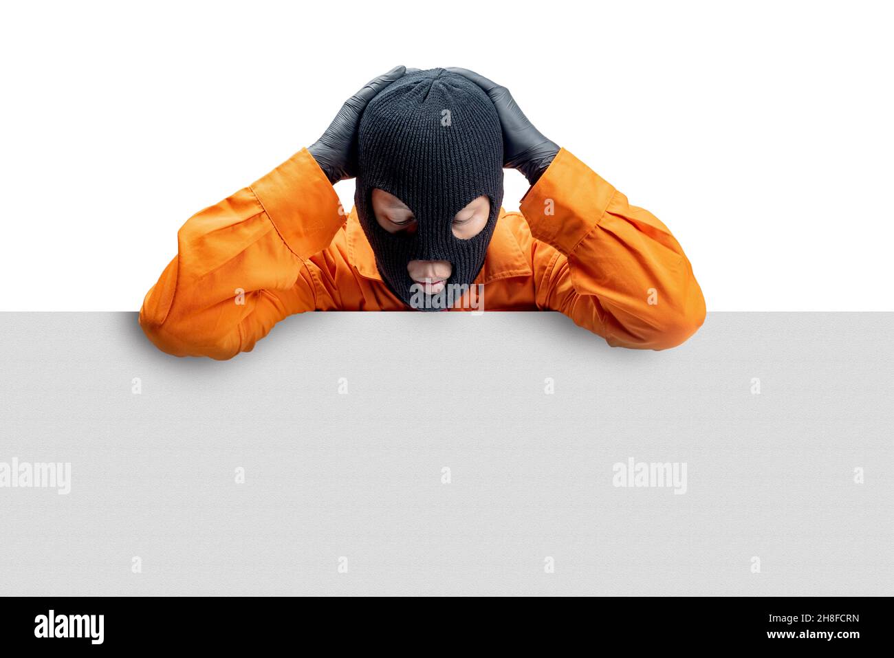 A criminal man in a hidden mask standing behind a white wall isolated ...