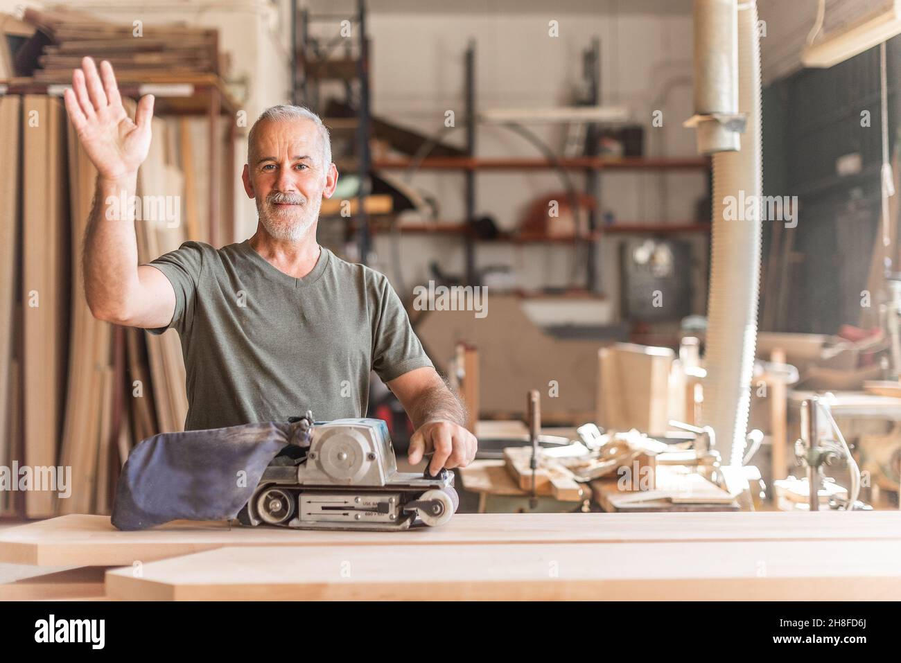 Smiling worker waving with a hand sander machine Stock Photo - Alamy