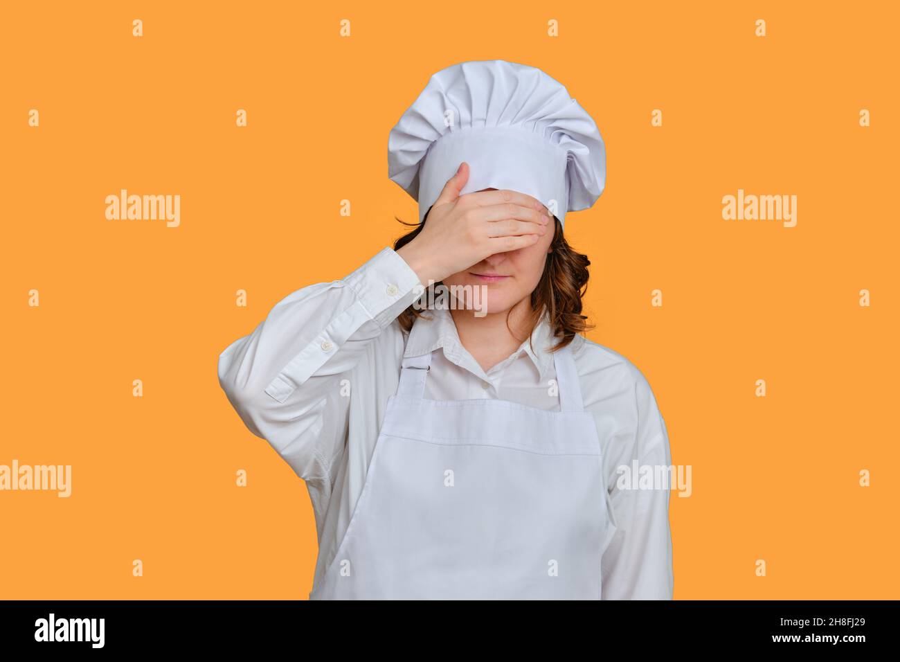 Confused woman chef is sad with hands to face on studio background ...
