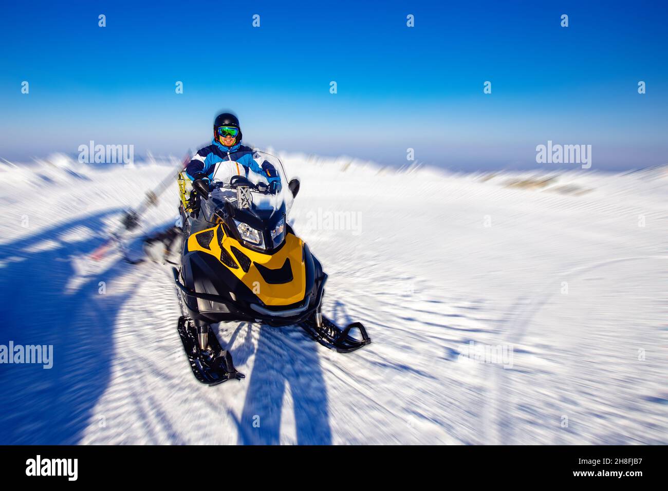 Happy snowmobile driver on blue sky background, motion blur effect ...