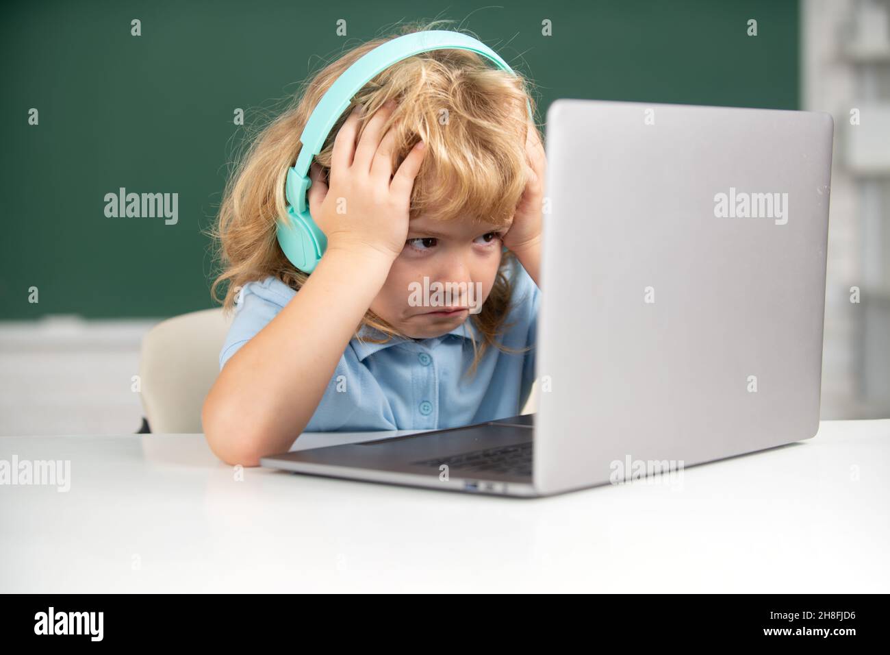 Angry sad boy in headphones sit at desk, study online on laptop at ...