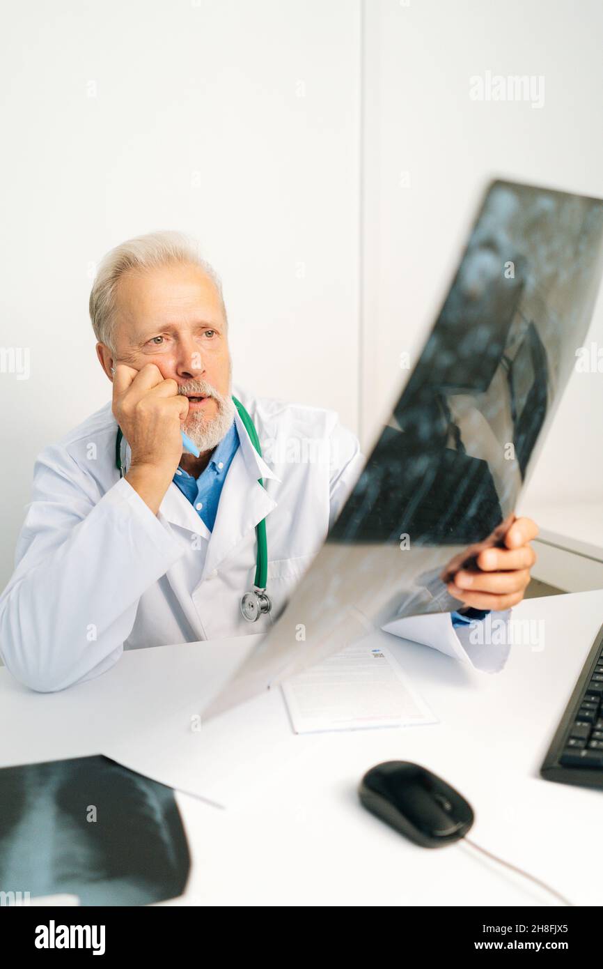 Vertical shot of focused mature male doctor examining head MRI scan of ...