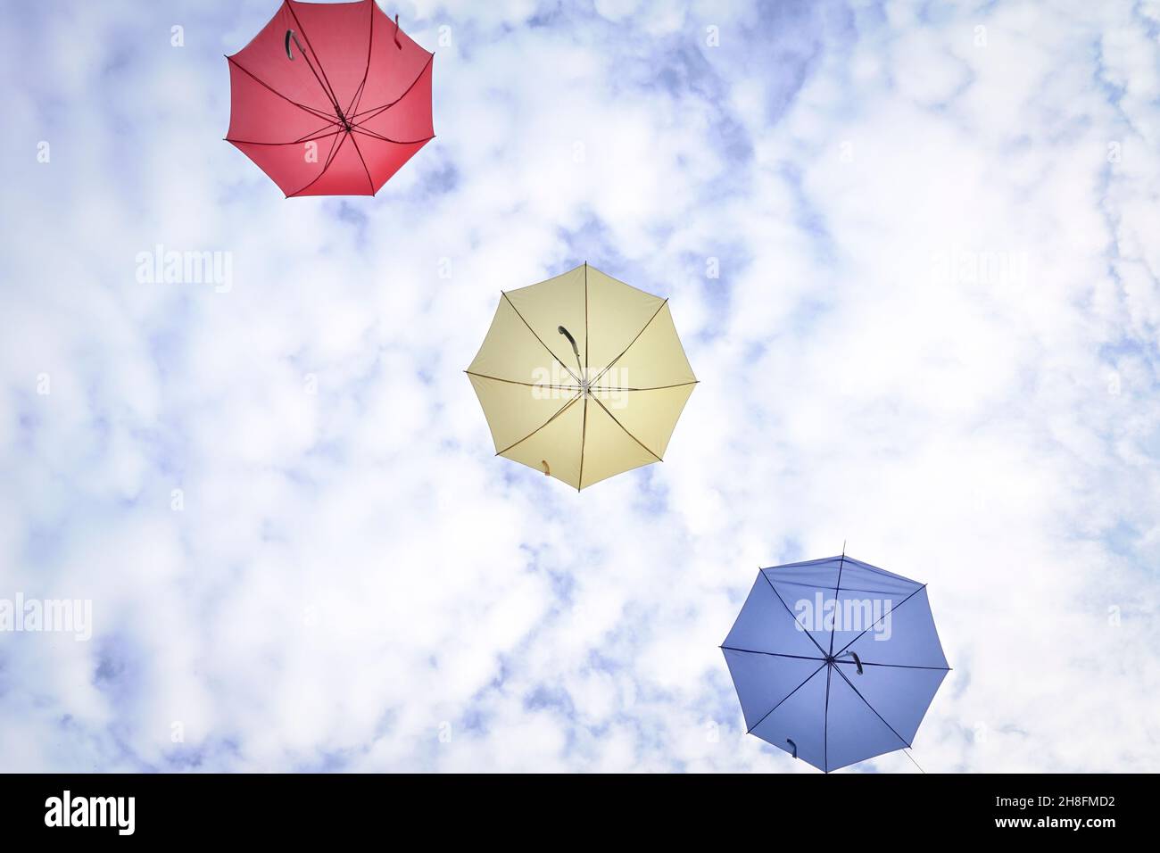Three umbrellas, red, yellow and blue colors on blue sky with clouds ...