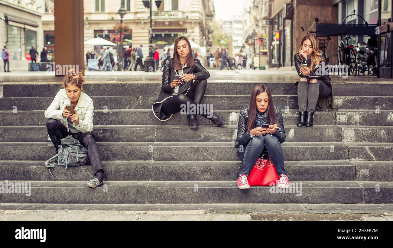 Group of girls sitting on the city stairs with smartphone. Technology ...