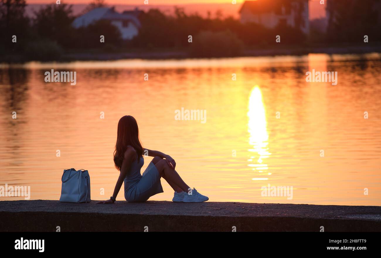 Lonely woman sitting alone on lake shore on warm evening. Solitude and ...