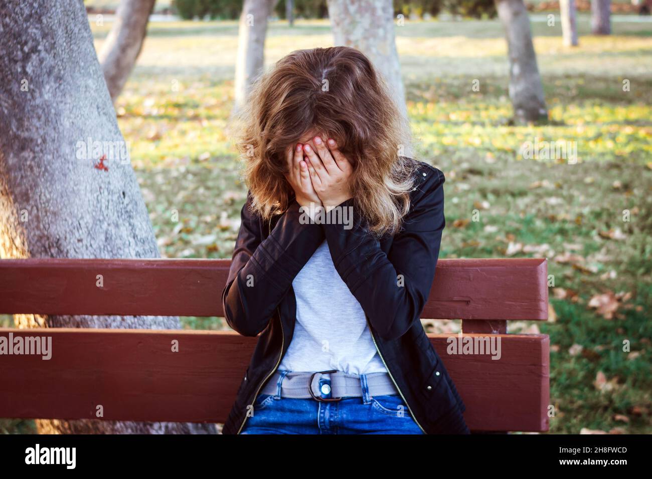 Sad teenager girl sitting on the bench in autumn park. Crying young ...
