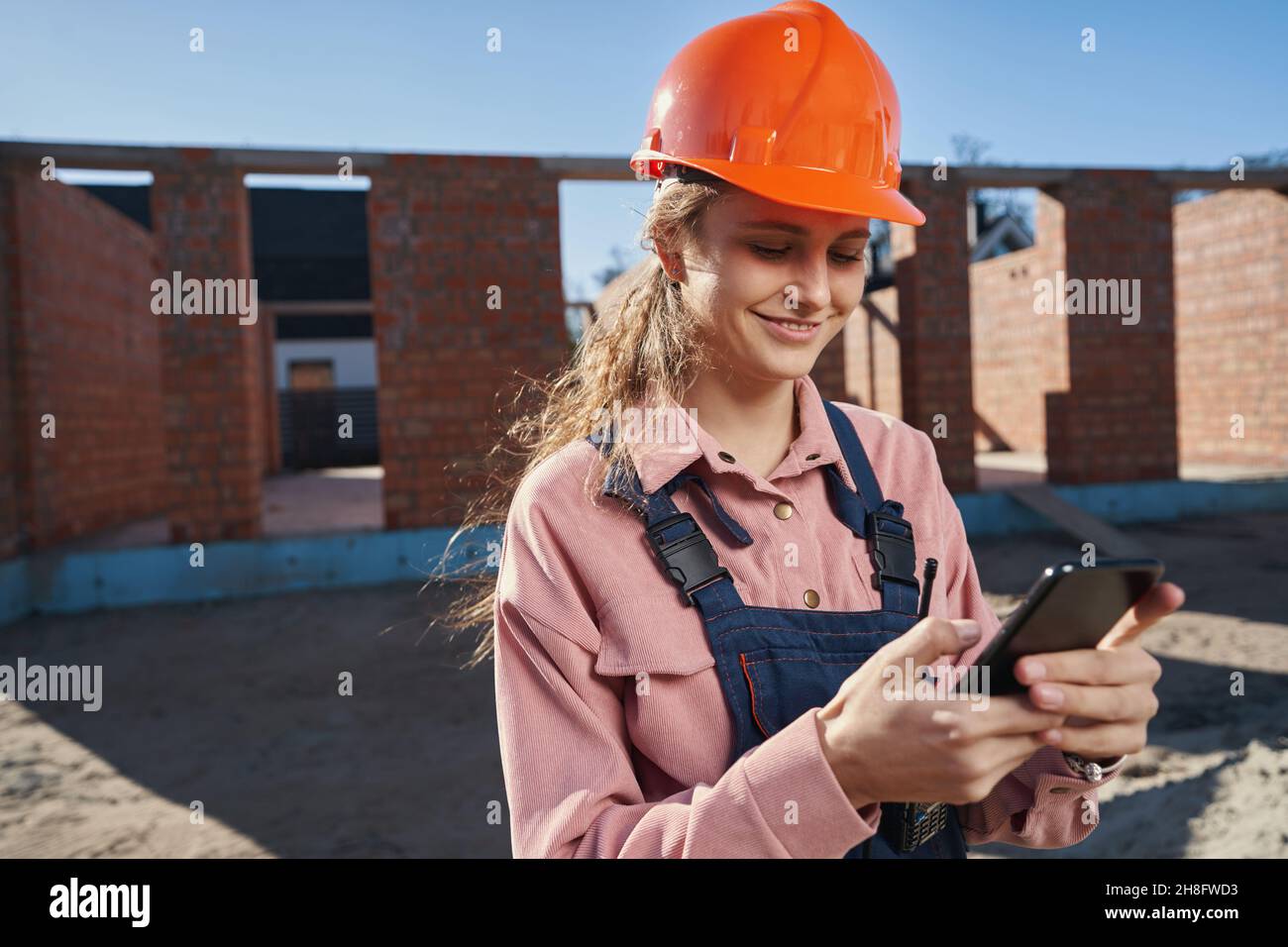 Young female builder holding smartphone in construction area Stock ...