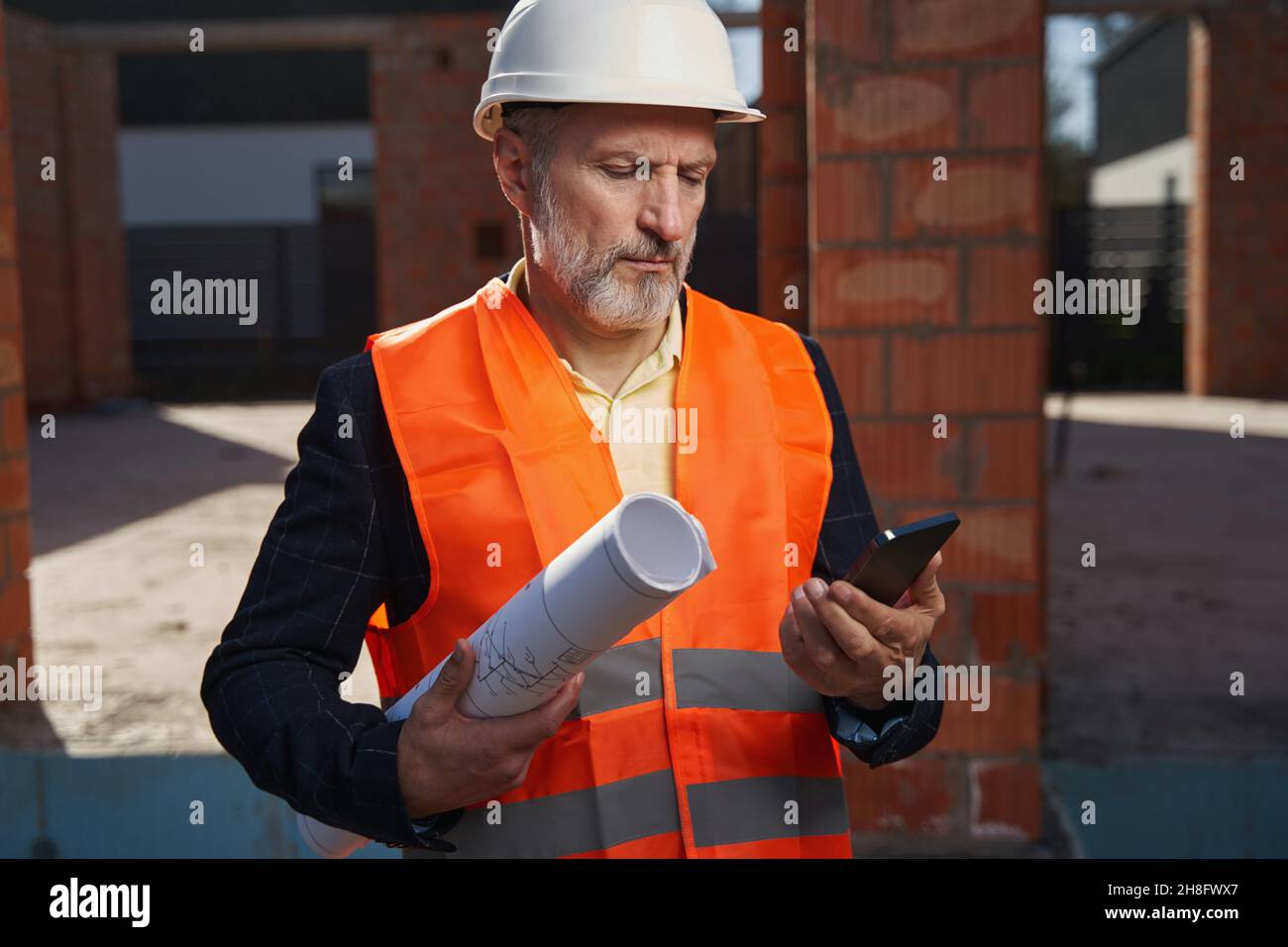Dedicated builder bringing construction plans and checking his phone ...
