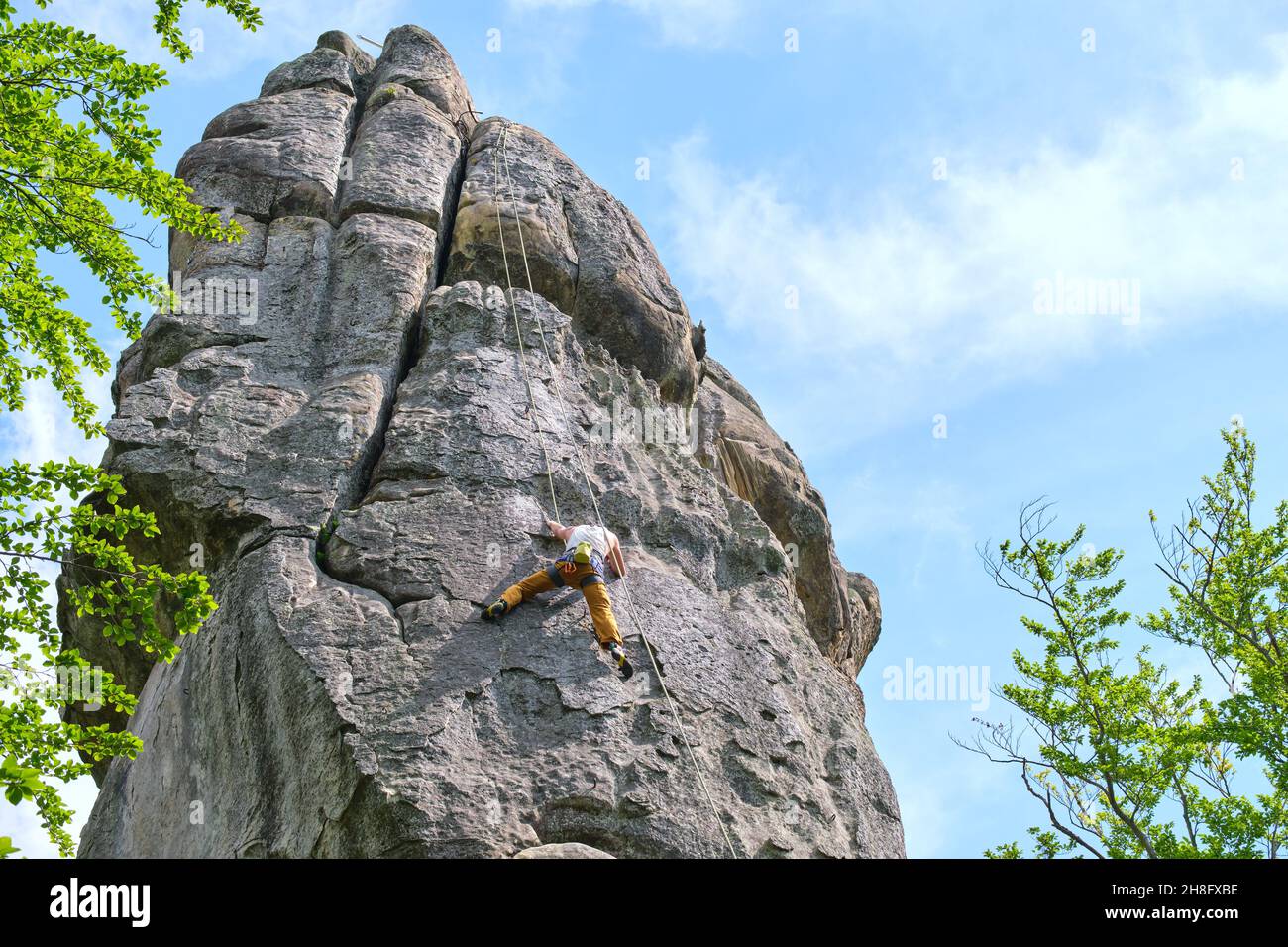 Young man climbing steep wall of rocky mountain. Male climber overcomes ...