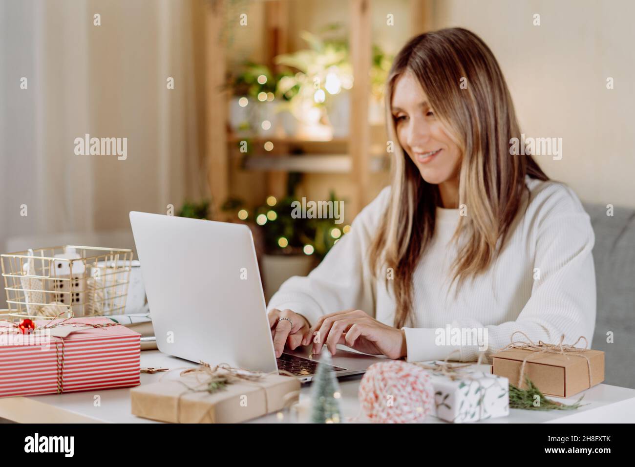 Happy and smiling woman wrapping and preparing Christmas gifts, typing ...