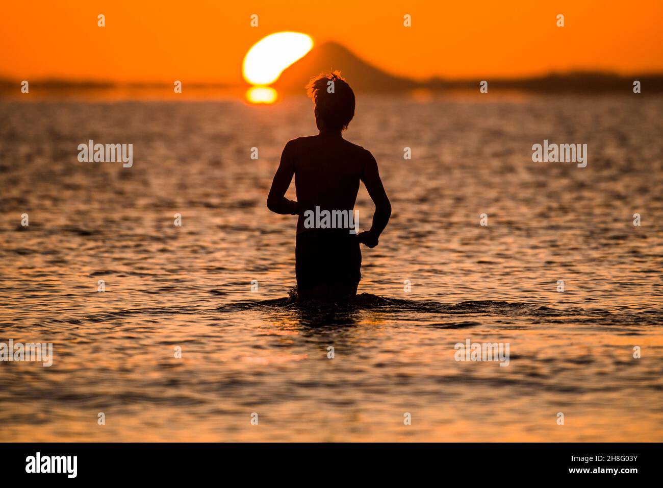 A wild swimmer walks into the cold waters as the sunrises behind North ...