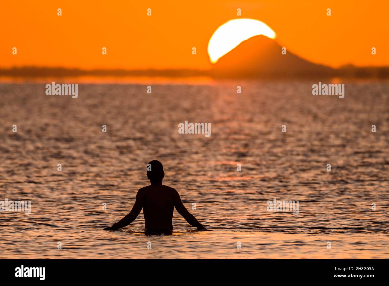 A wild swimmer walks into the cold waters as the sunrises behind North ...
