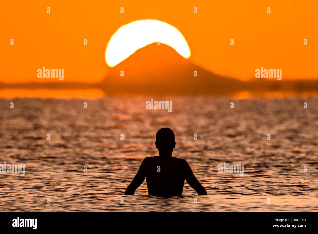 A wild swimmer walks into the cold waters as the sunrises behind North ...