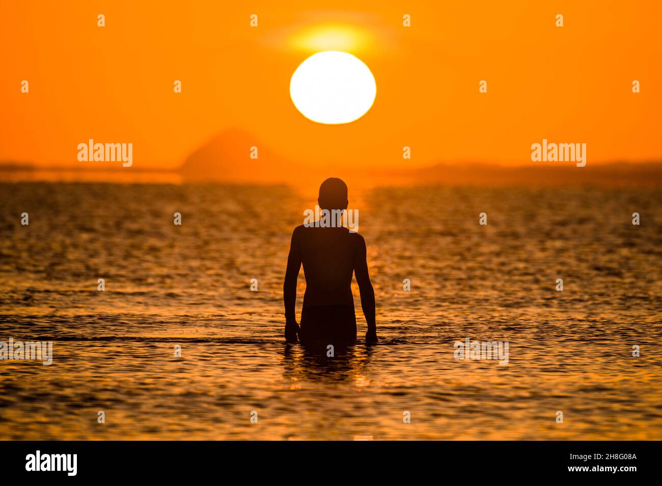 A wild swimmer walks into the cold waters as the sunrises behind North ...