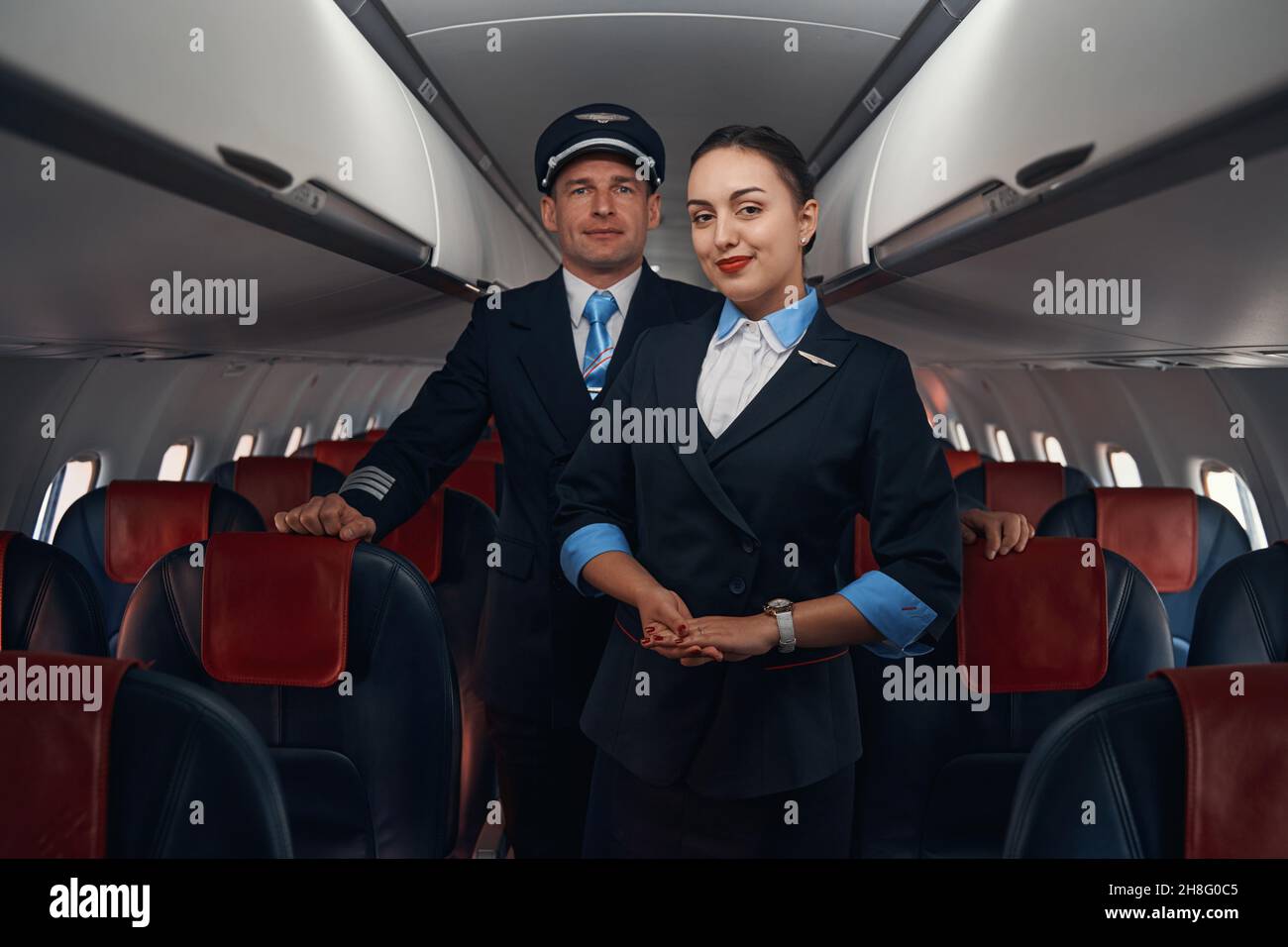 Satisfied flight attendant and pilot standing near passenger seats ...