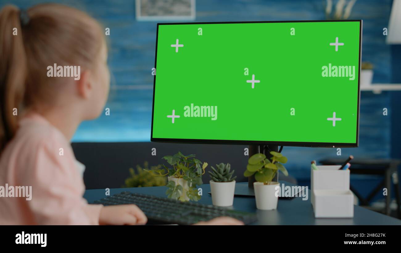 Young girl looking at monitor with horizontal green screen at desk ...