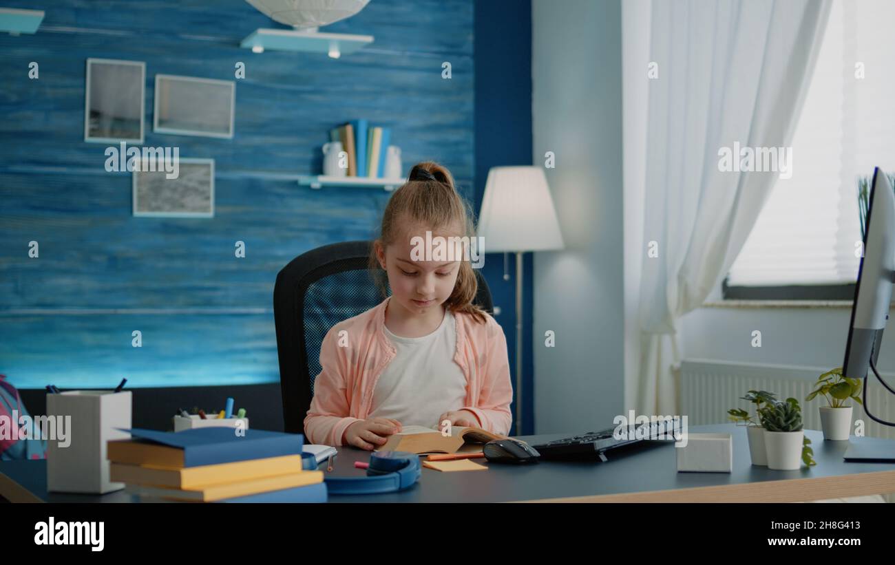 Caucasian girl reading book at desk for primary school work. Little ...