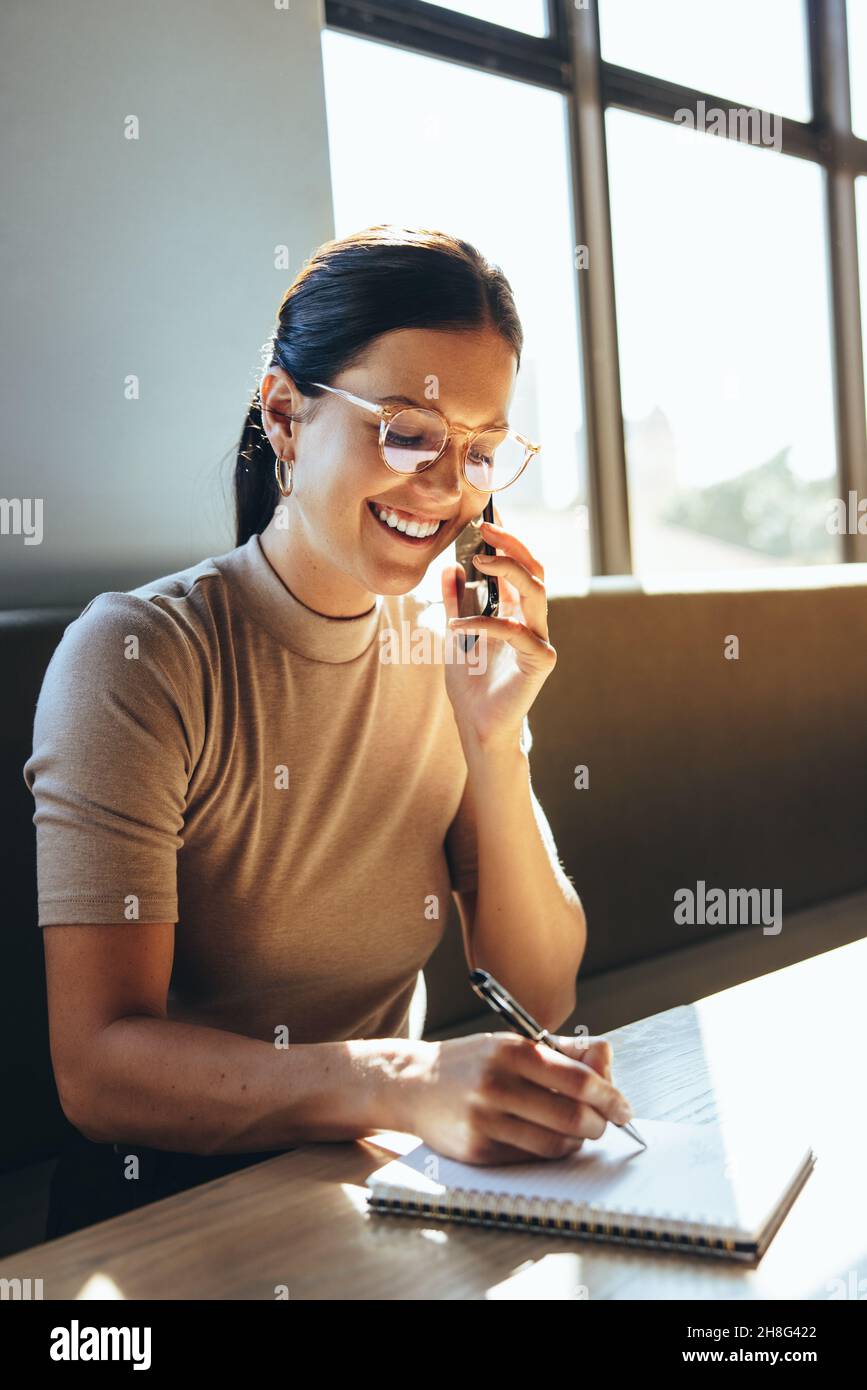 Making business plans over the phone. Happy young businesswoman writing ...