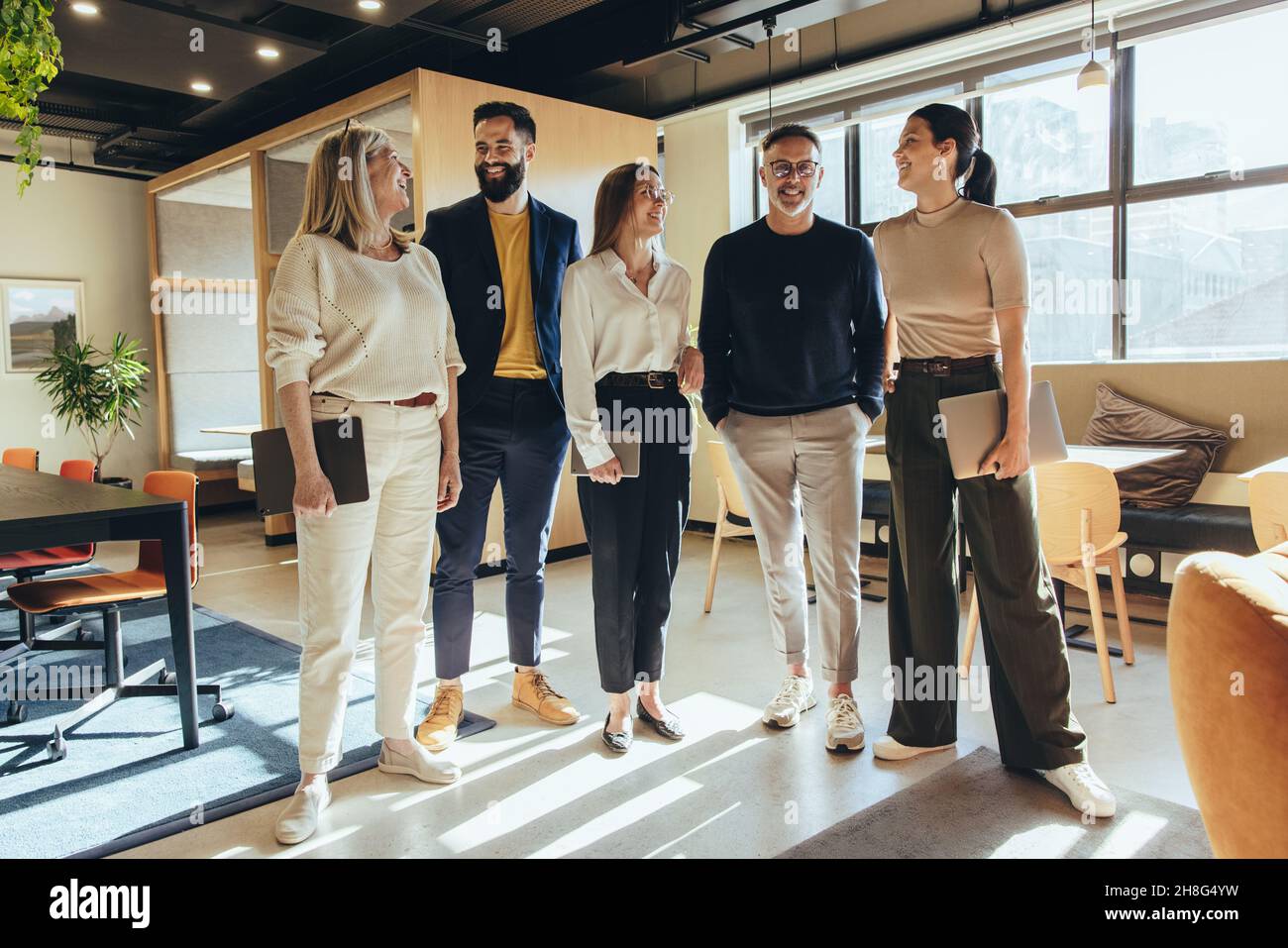 Group of happy colleagues smiling cheerfully while standing in an ... Group of happy colleagues smiling cheerfully while standing in an ...