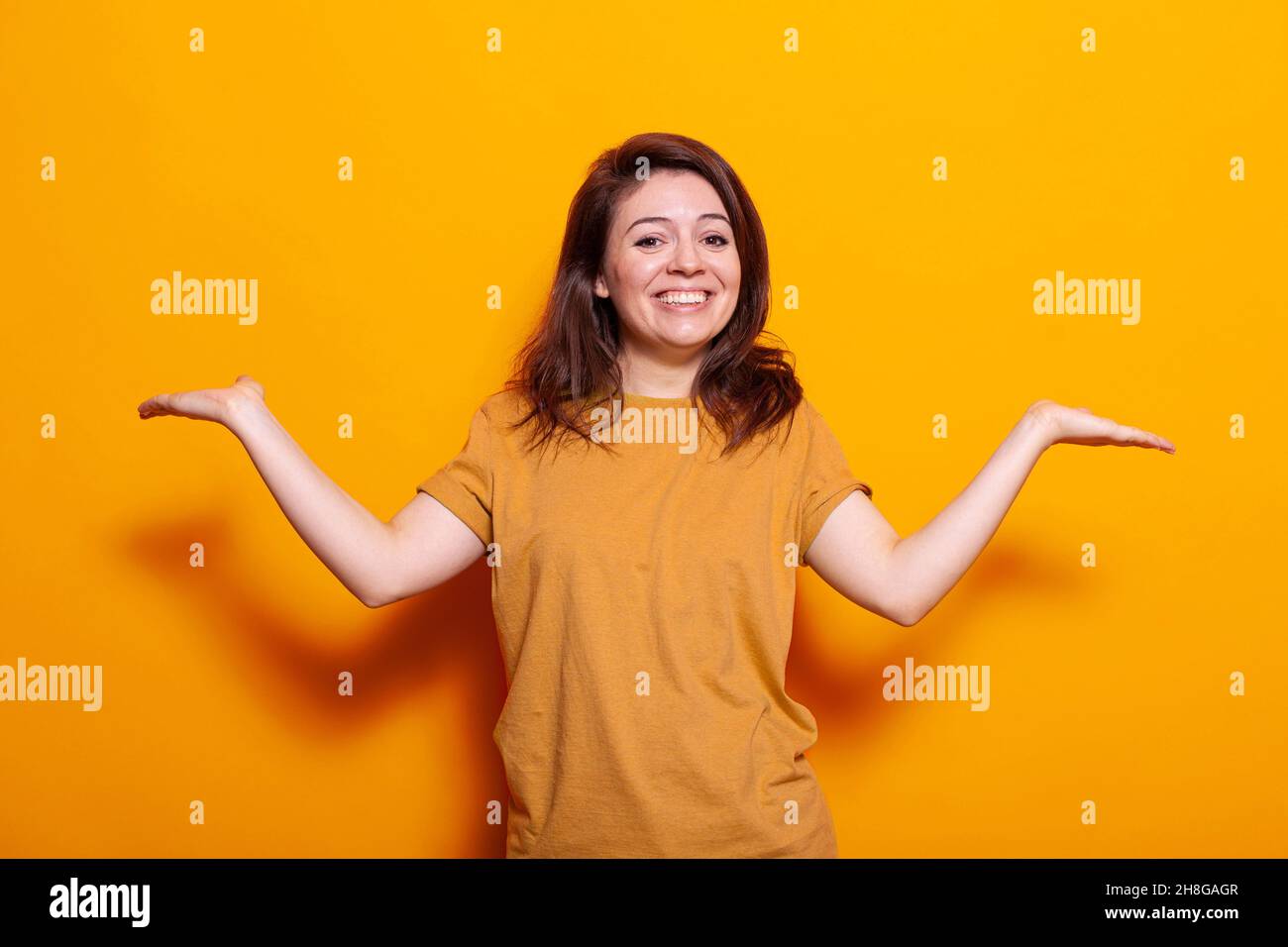 Portrait of confused woman raising hands and shoulders while smiling in ...