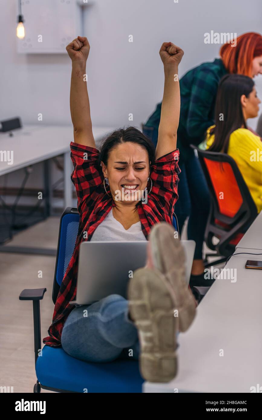 A young female worker with her hands up in the air, her legs on the ...