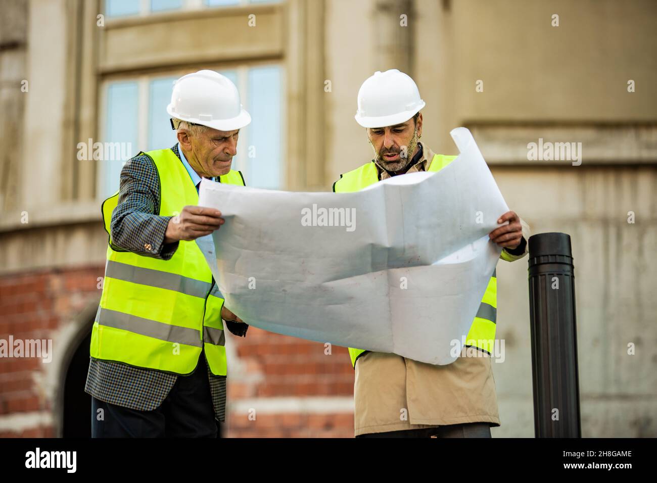 Two construction workers are looking at the plans on the paper Stock ...