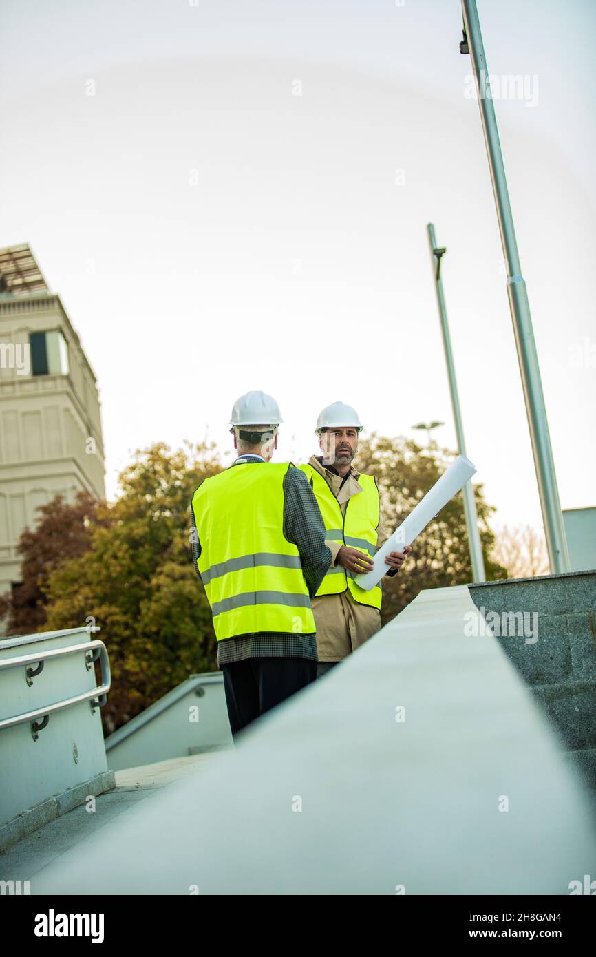 Two senior construction workers are looking and thinking while talking ...