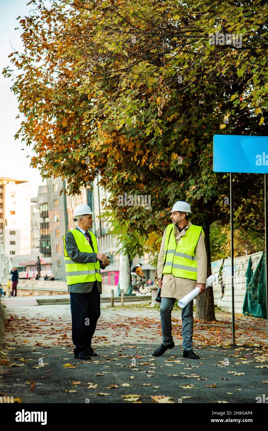 Two construction workers are walking together while talking to each ...