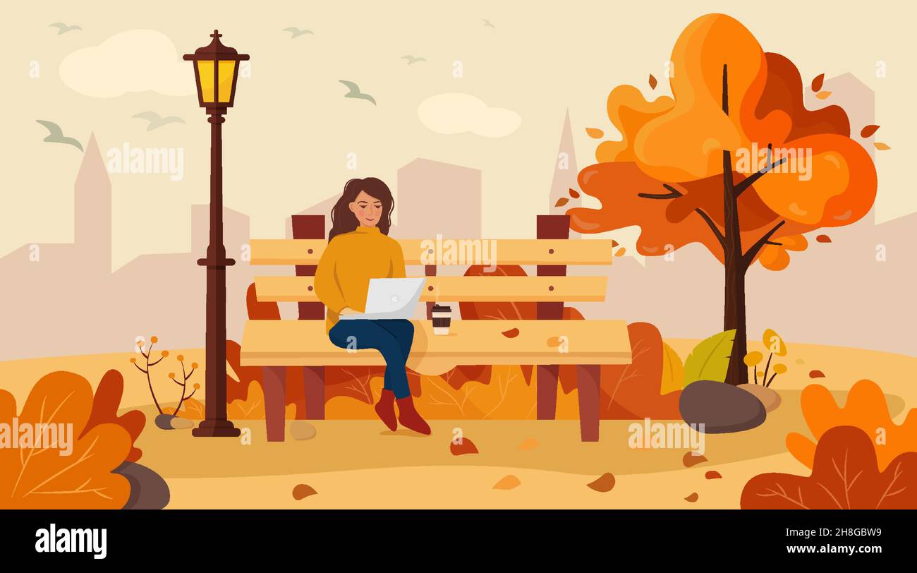 A girl sits on a bench in an autumn park and works at a laptop. Trend ...