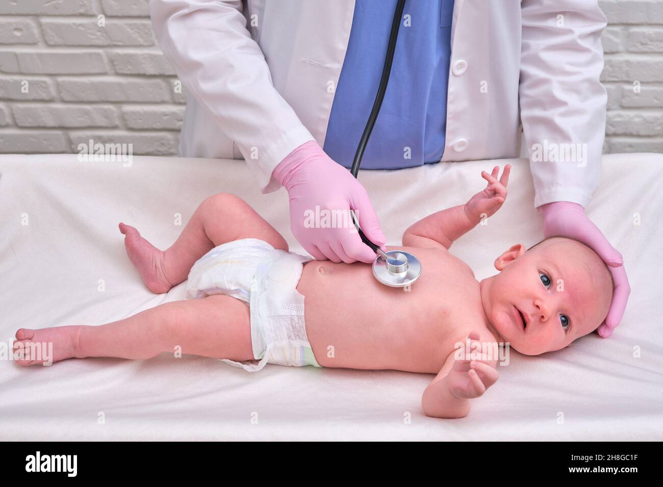 Woman doctor listens with a stethoscope to a newborn baby. Nurse checks ...