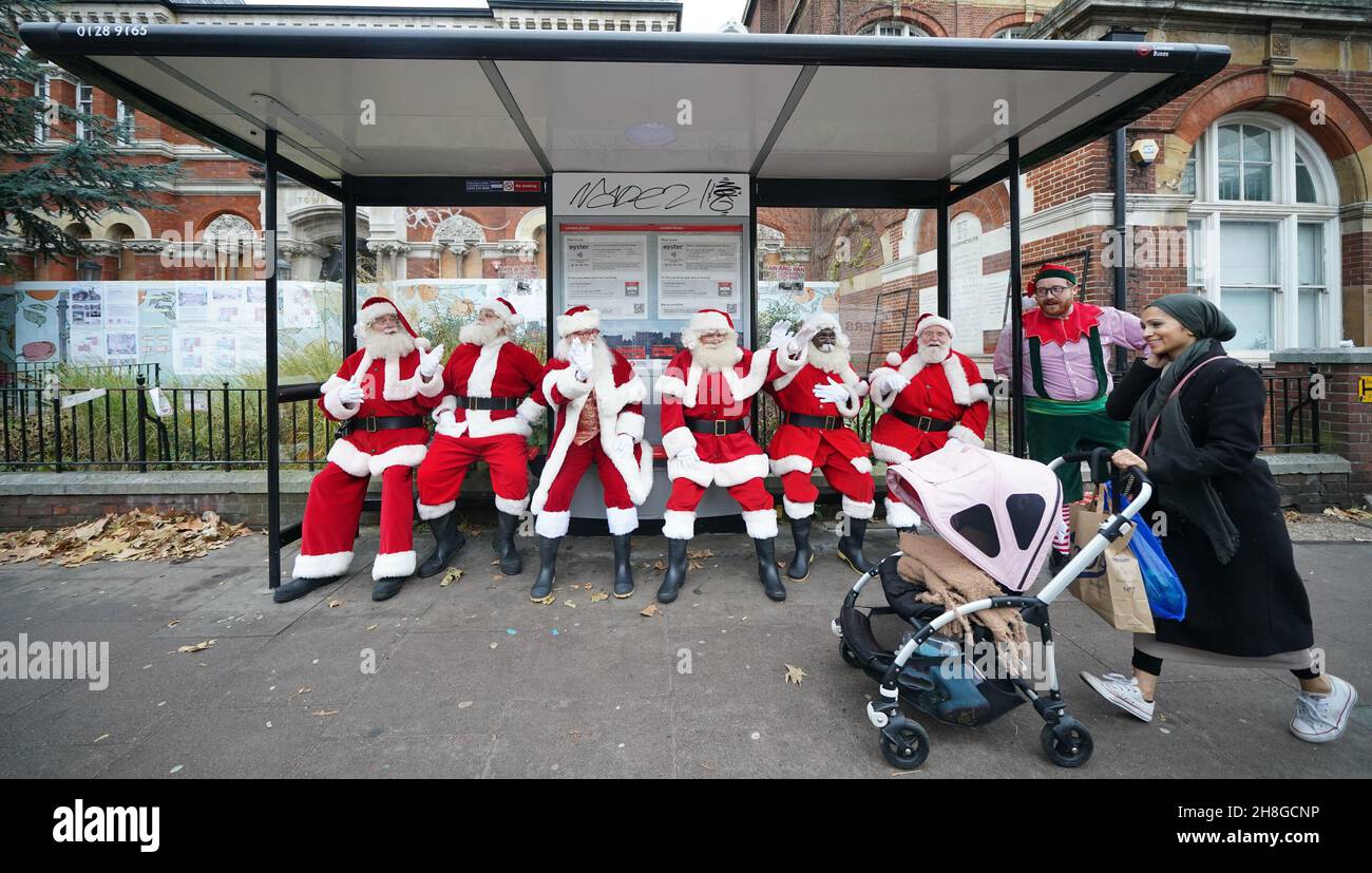 A woman pushes a pram past student santas and an elf waiting at a bus ...