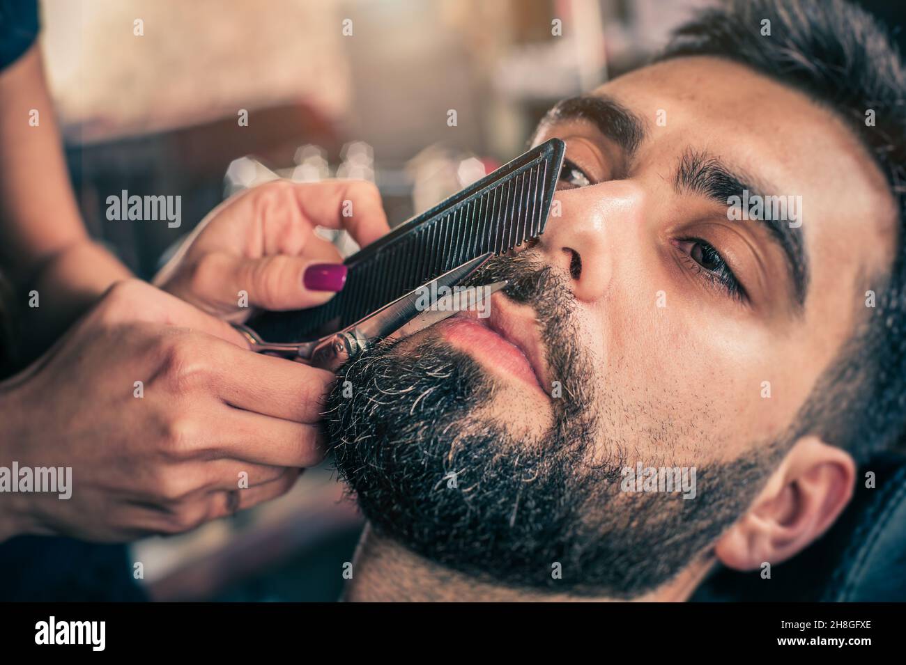 Female barber beard cut a client's beard with clippers in a barber shop ...