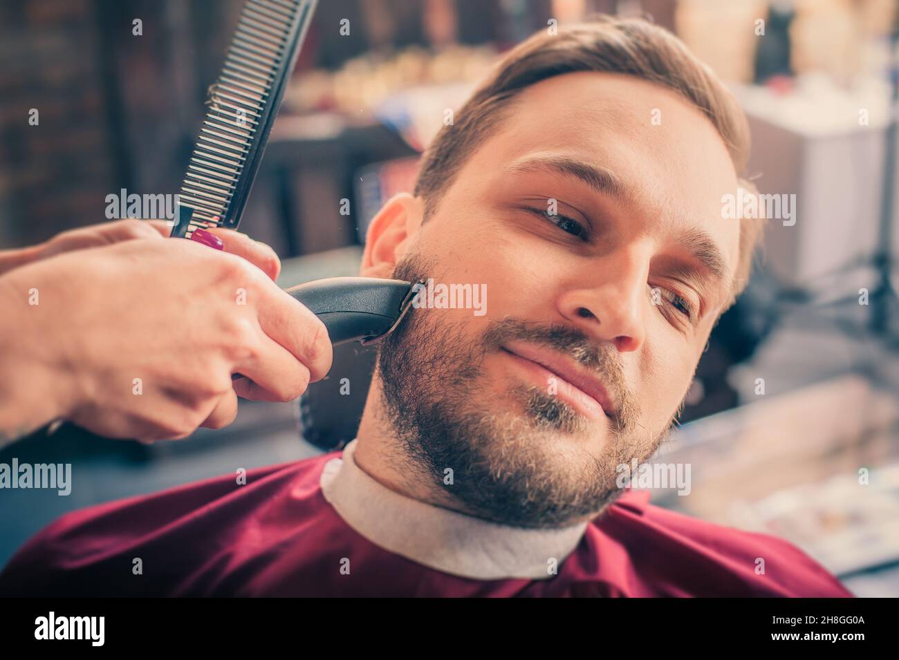 Female barber shaving a client's beard with trimmer in a barber shop ...