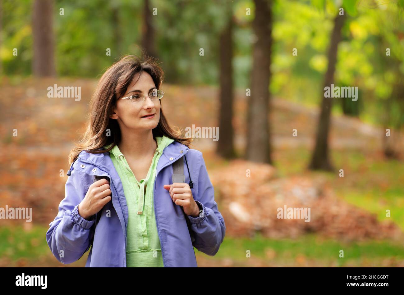 Middle aged active caucasian female model with backpack walk in woods ...
