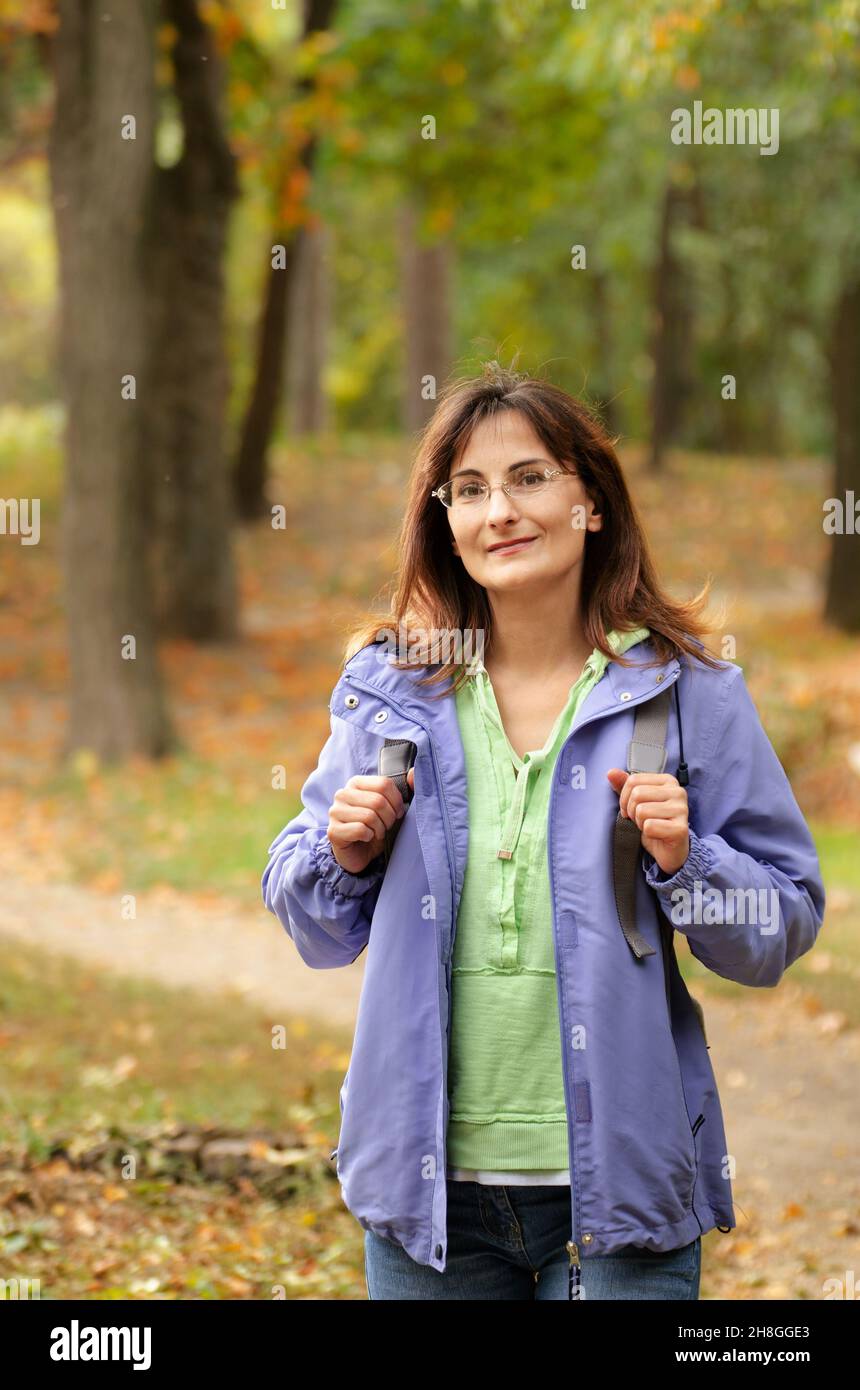 Middle aged active caucasian female model with backpack walk in woods ...