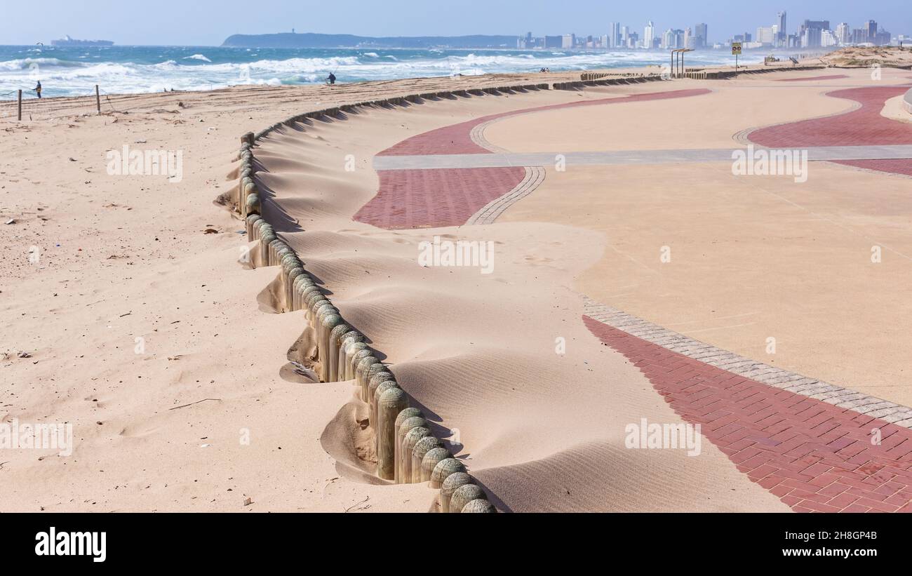 Beach shifting sand blows over low placed wood roles onto promenade ...