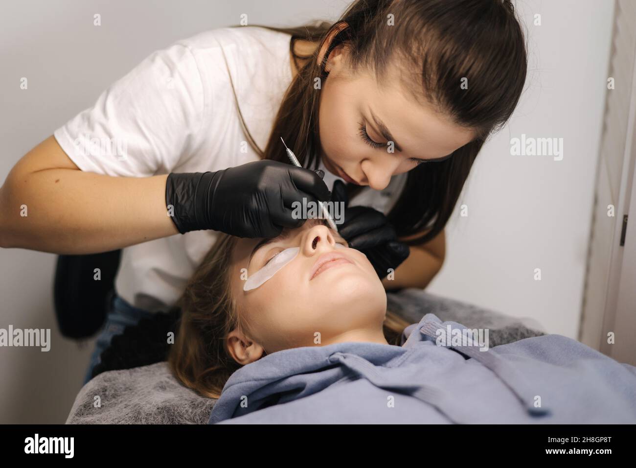 Beautician making eyelash lamination procedures for young model. Modern ...