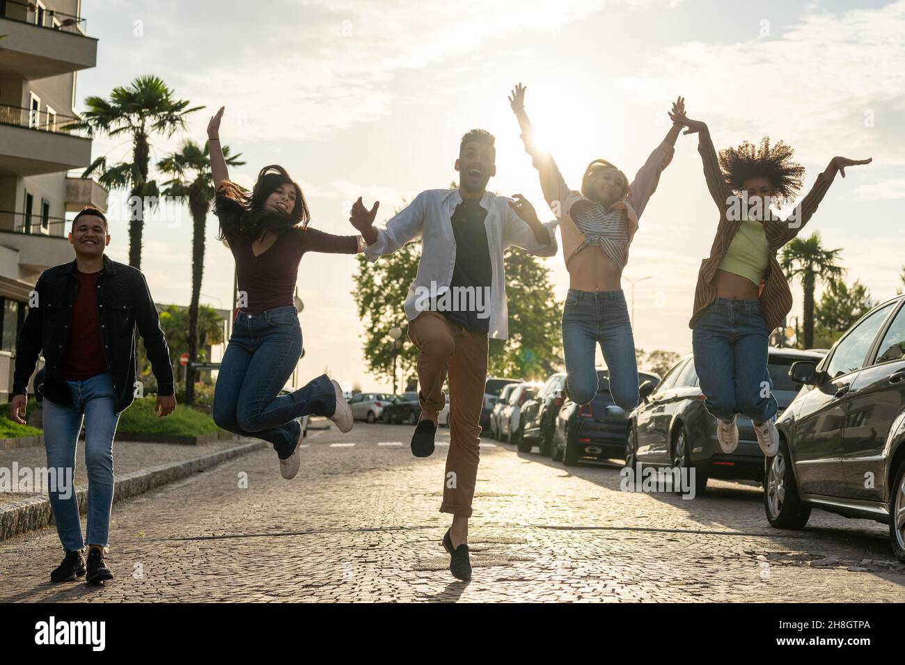 group of young people jumping and laughing in a city street, happy ...