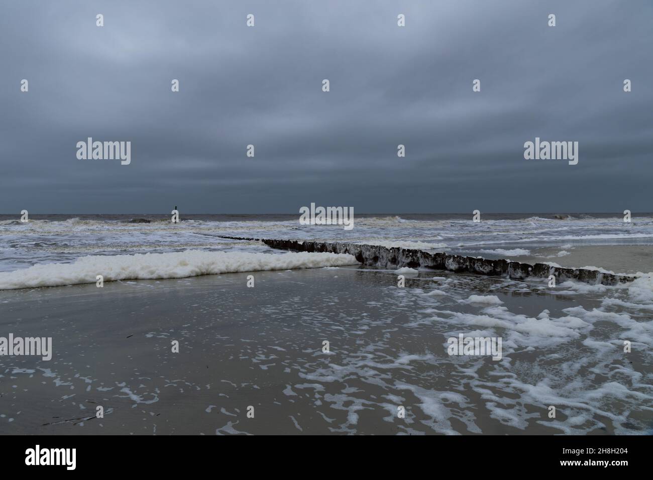 Dark skies and rough surf with an abundance of sea foam along a metal ...